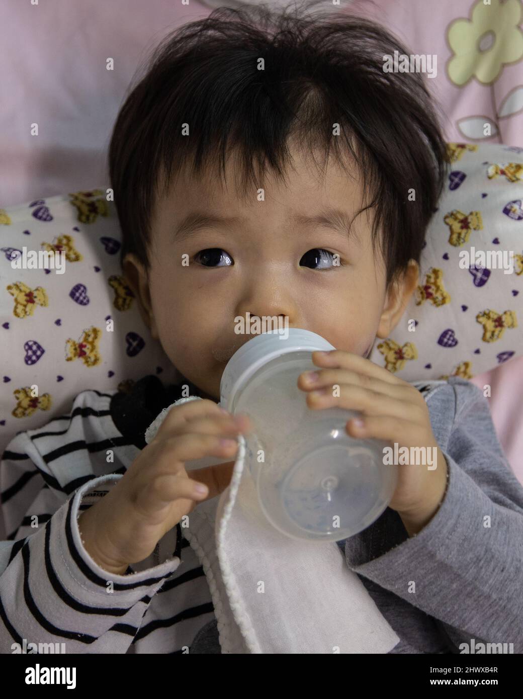 Asian Chinese baby boy lying on bed with holding a milk bottle drinking ...