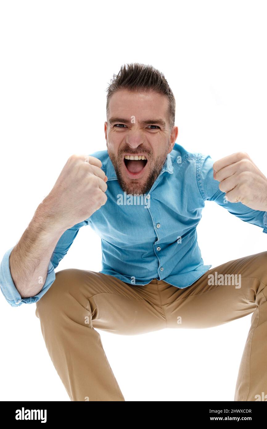 low angle view of excited guy with chino pants holding fists up ...