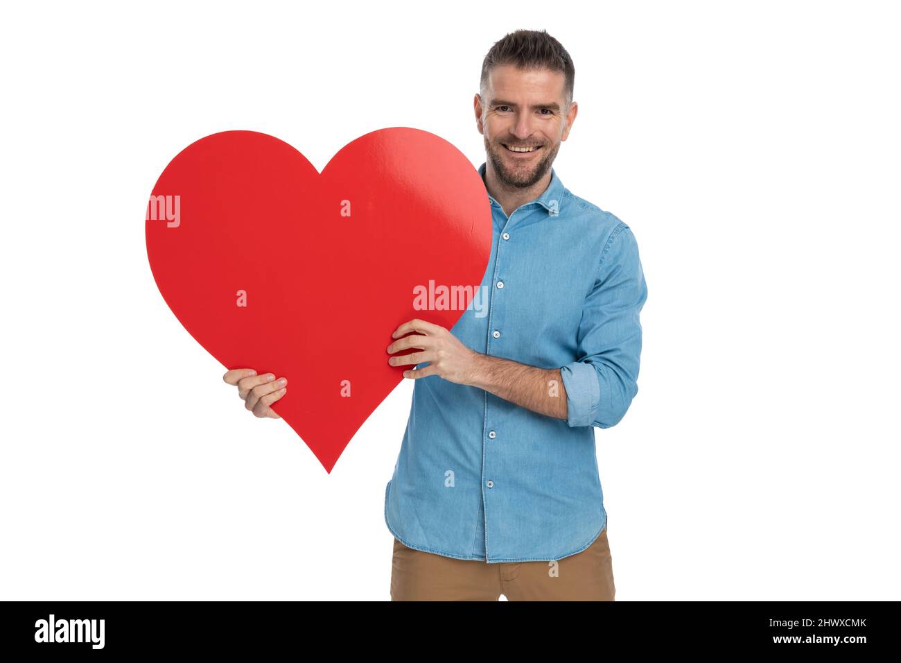 happy young man in denim shirt smiling, holding big red heart, being ...