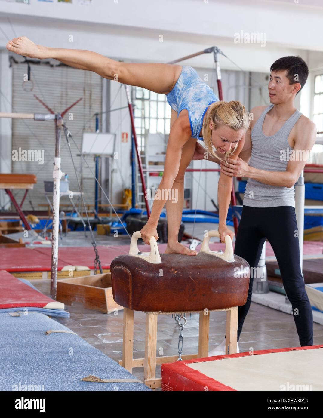 Woman in bodysuit exercising action at vaulting hourse in gym, man ...