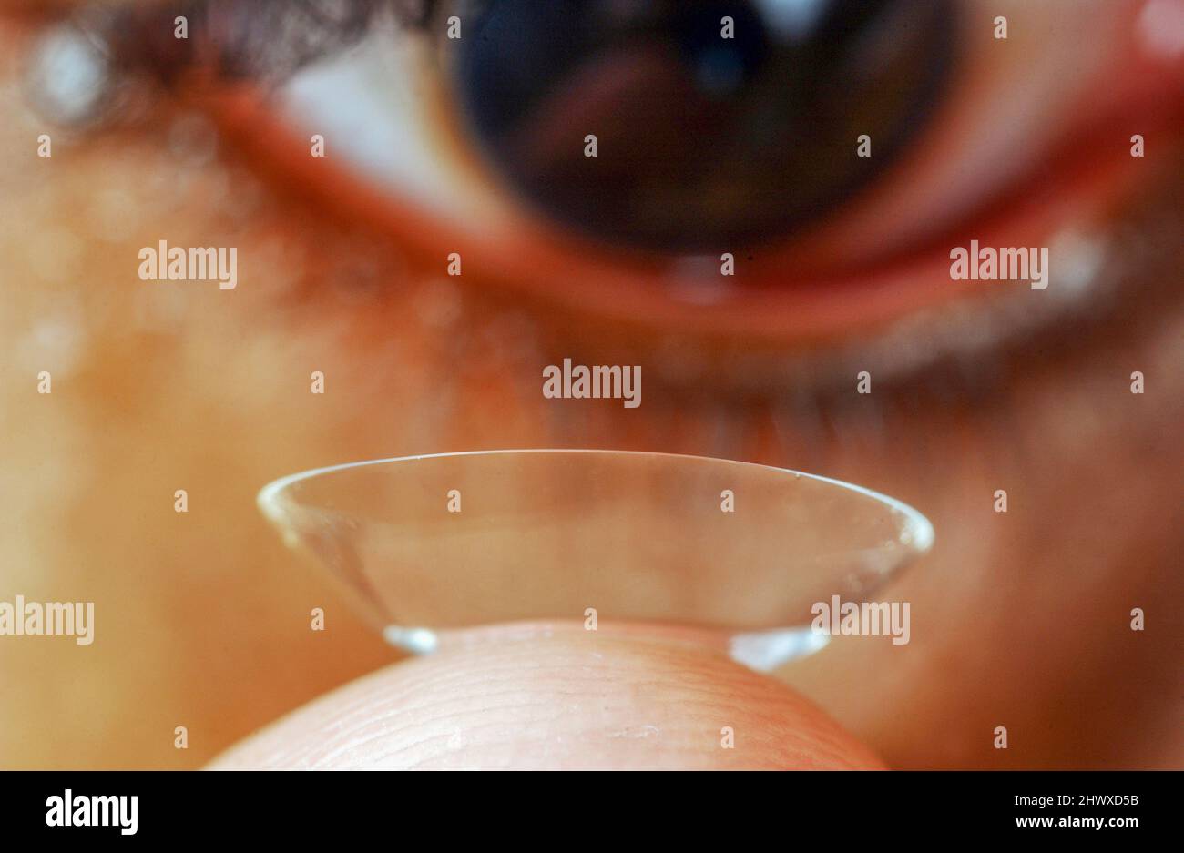 A facial close up of a young man putting a contact lens onto his eye ...