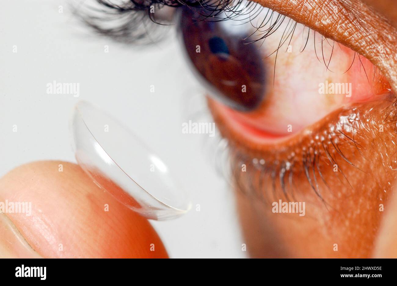 A facial close up of a young man putting a contact lens onto his eye ...