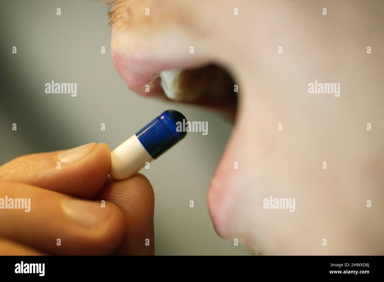 A young man places a blue and white tablet into his mouth Stock Photo ...