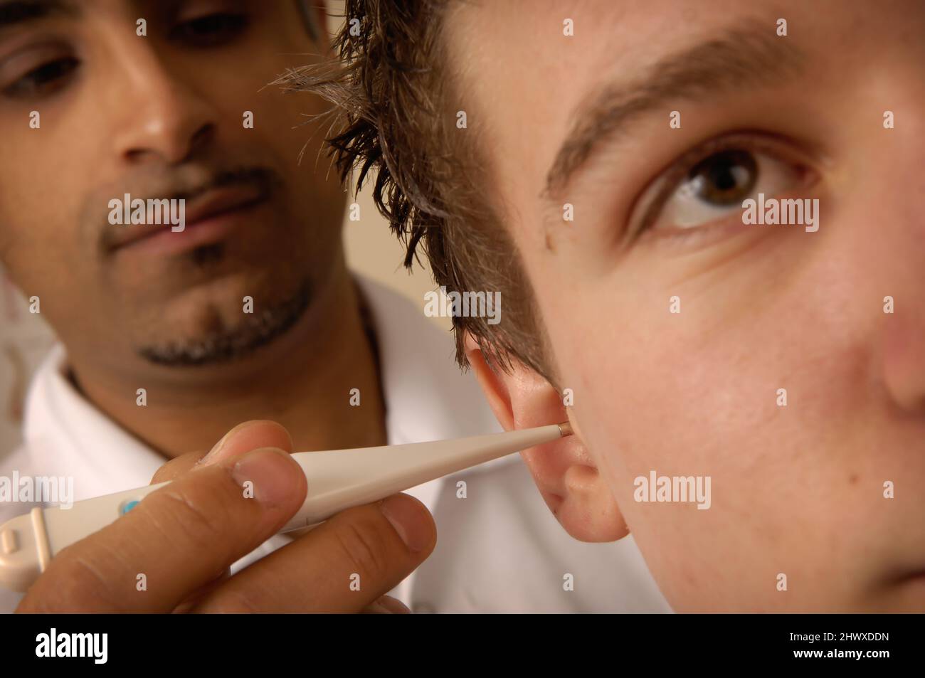 A clinician takes a patient’s aural temperature with a digital ...
