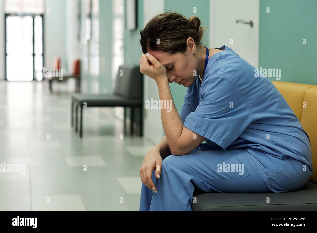 Young tired or stressed female doctor in uniform sitting in hospital ...