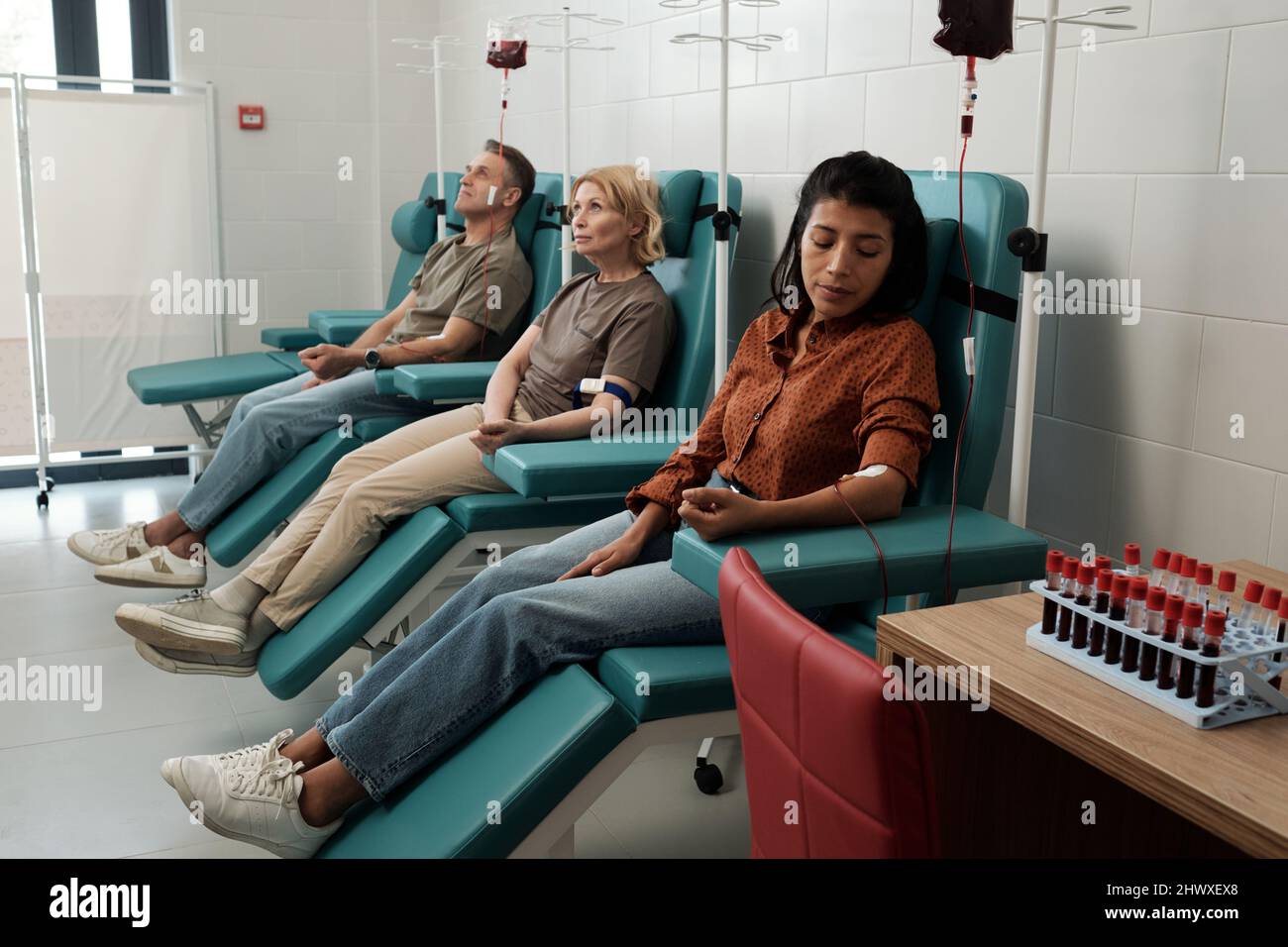Group of blood donors with dropper tubes sitting in row on chairs in ...