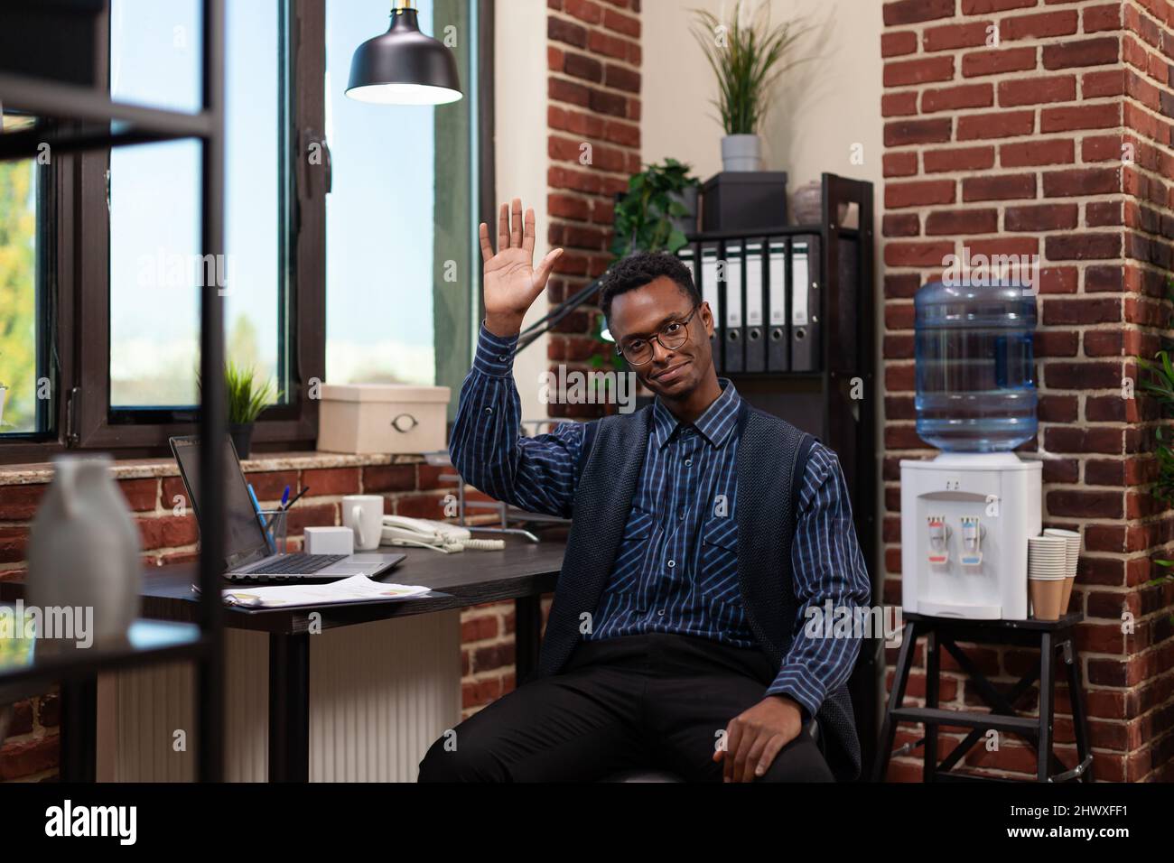 Confident startup employee sitting at desk with laptop waving hello in ...