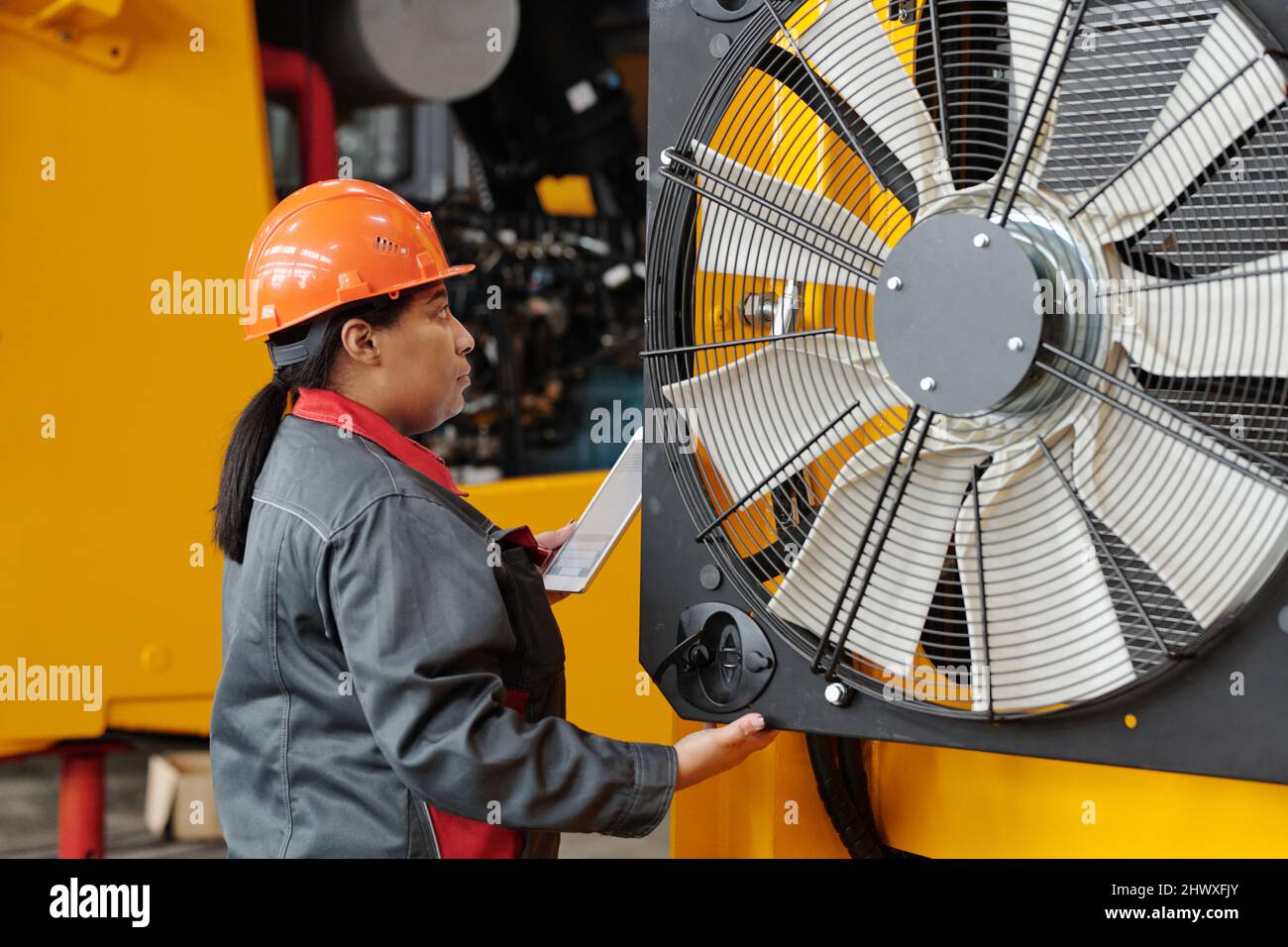 Young repair person in workwear and safety helmet checking air mover of ...