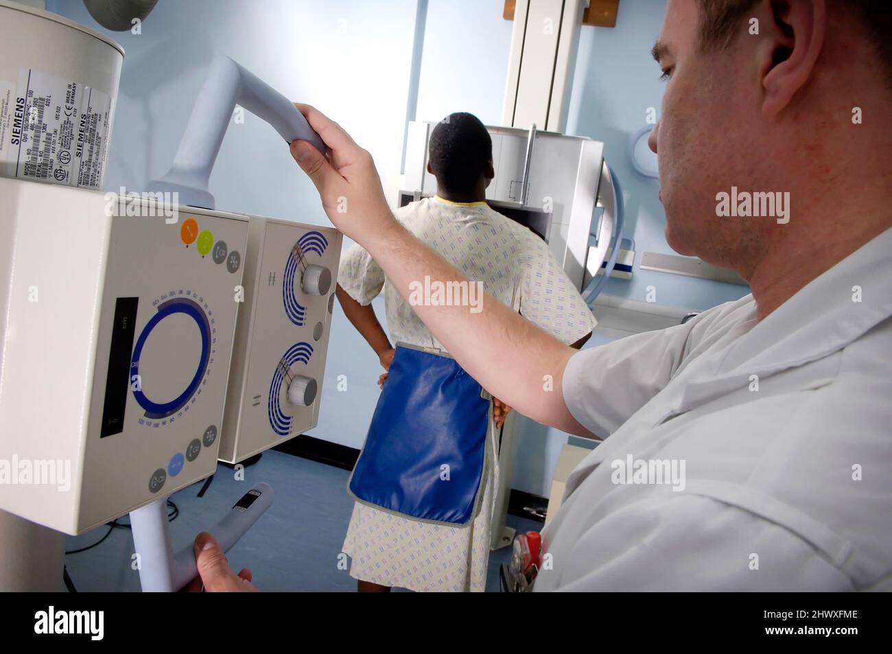 A radiologist x-rays a male patient who is standing in front of the x ...