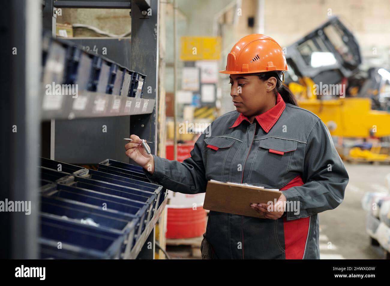 Serious young workwoman in safety helmet and uniform making revision of ...