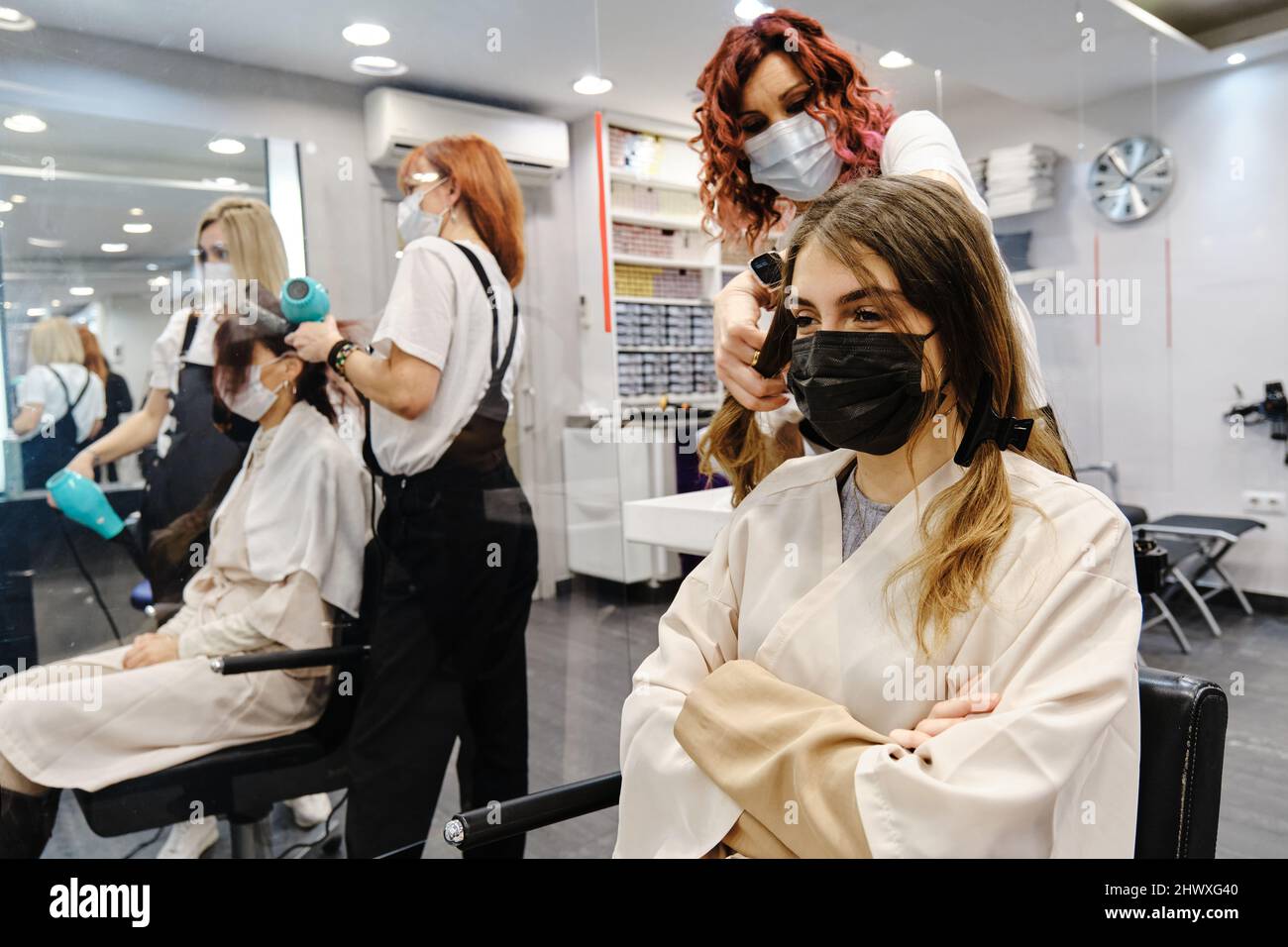 Young woman with a face mask getting a new hairstyle at the hair salon ...