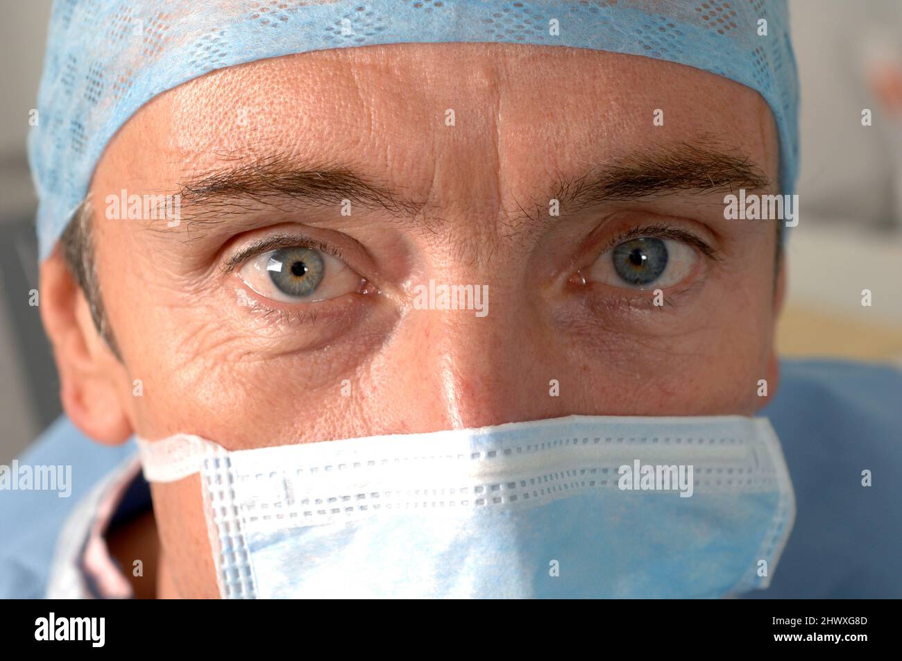 A close-up of the staring eyes of a male surgeon wearing a blue ...