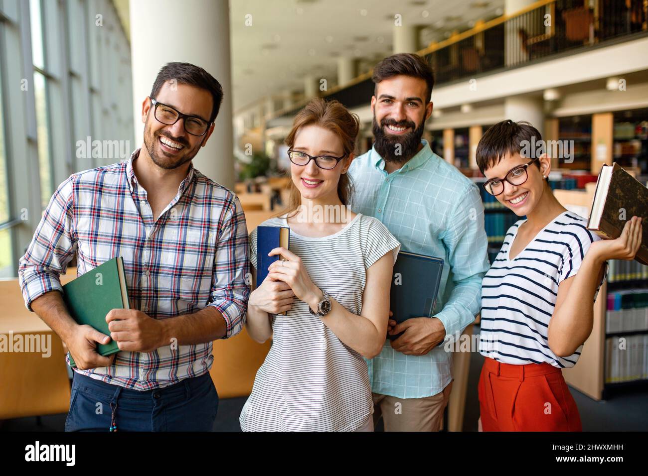 Happy university students studying with books in library. Group of ...