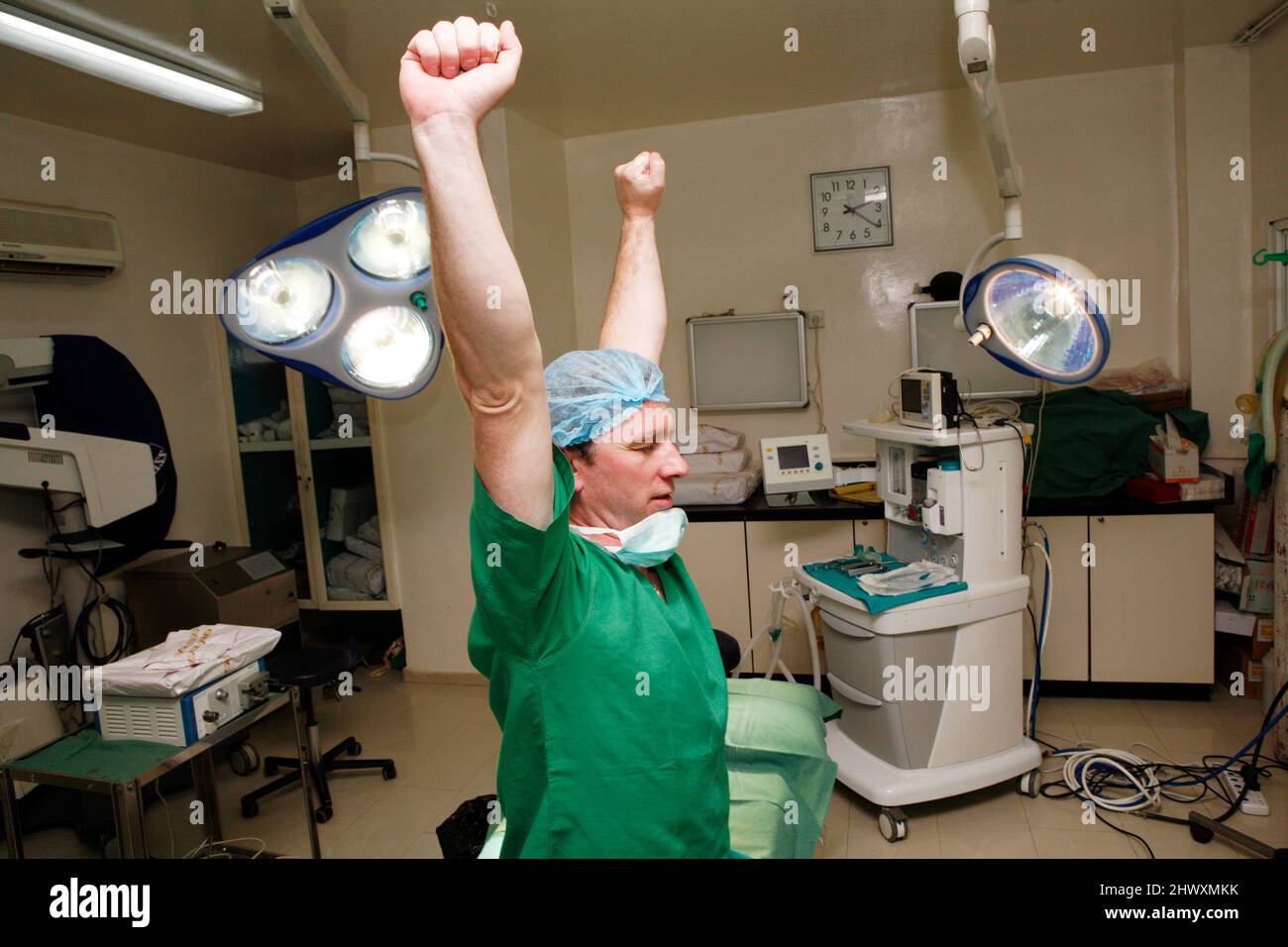 A tired overworked surgeon stretches his arms out as he sits on a ...