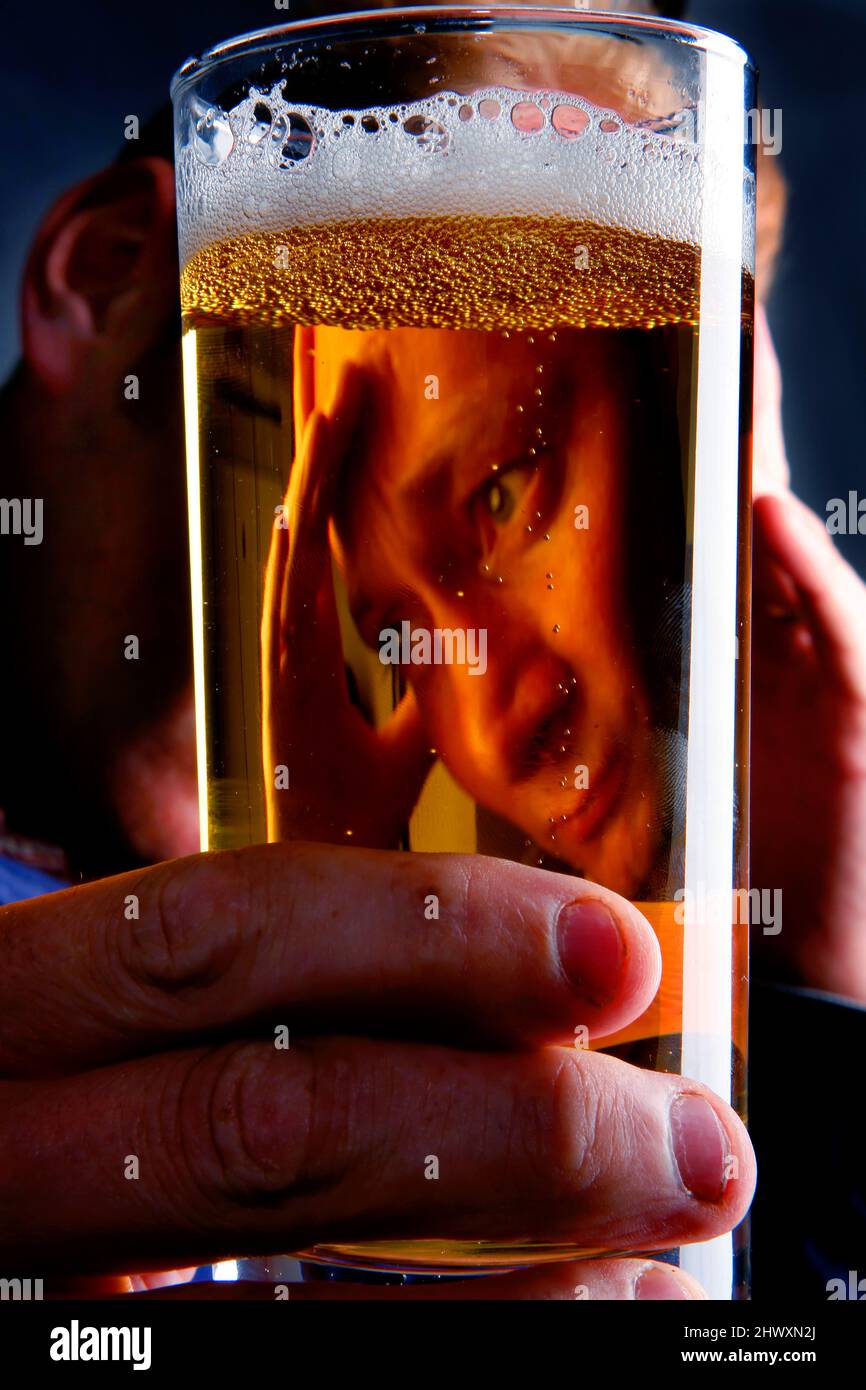 A depressed man's face is reflected in the glass of beer, which he ...