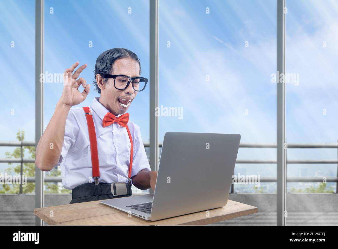 Asian nerd with an ugly face using laptop inside the room with a window ...