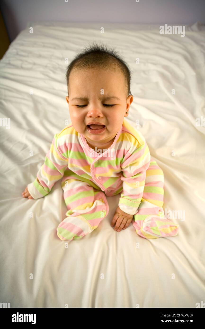 A baby girl sitting on a bed crying (MODEL RELEASED Stock Photo - Alamy