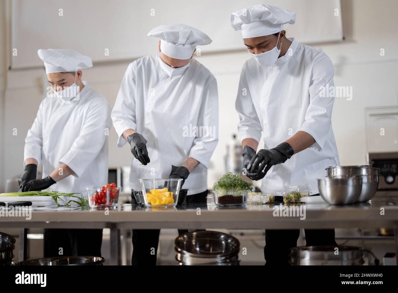 Three well dressed chefs in face masks prepare takeaway food in ...