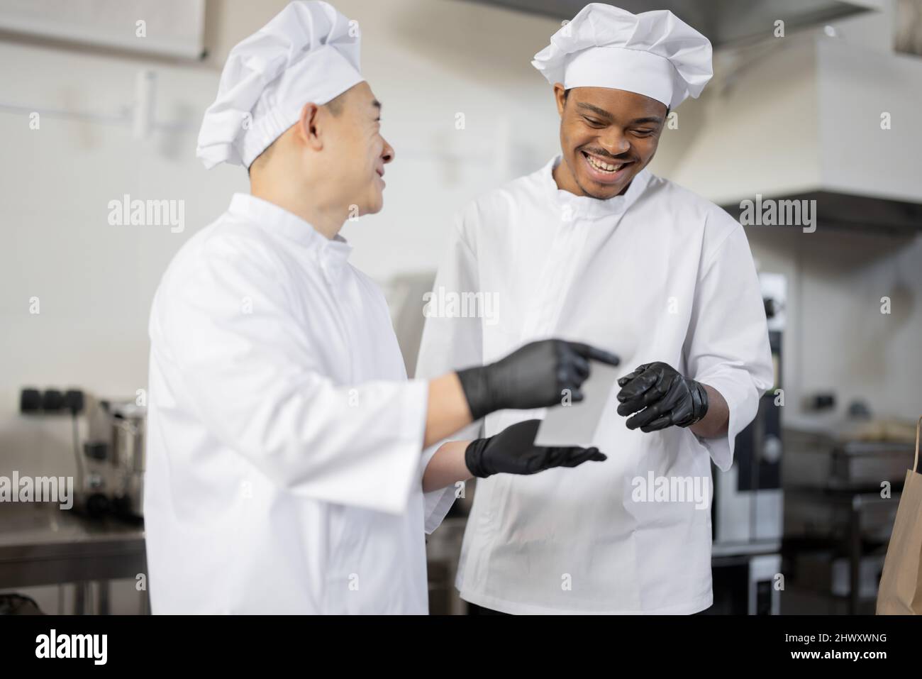Asian and Latin chefs reading printed order while cooking meals in ...