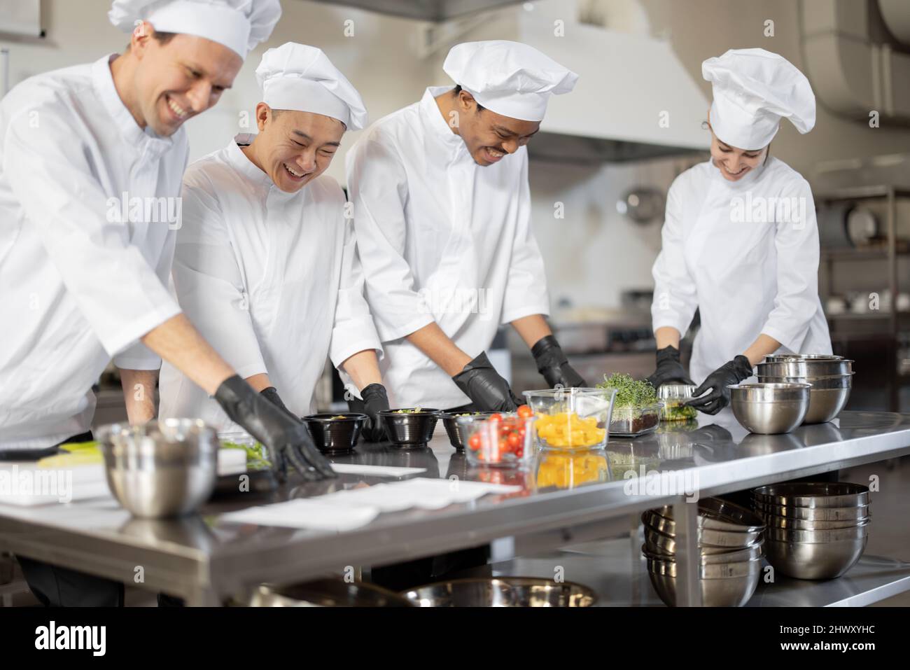 Multiracial team of cooks mixing ingredients for take away food in ...