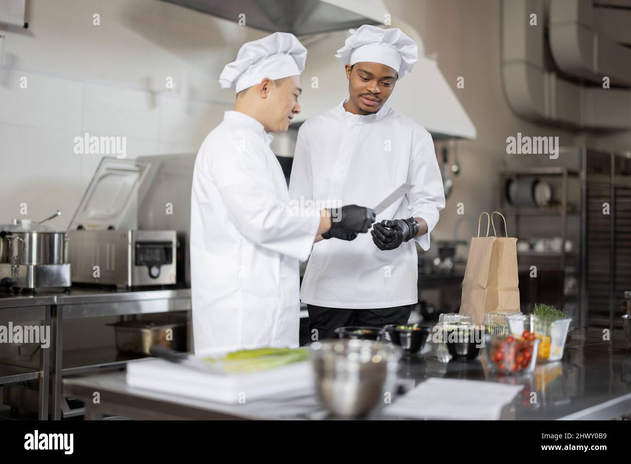Asian and Latin chefs reading printed order while cooking meals in ...
