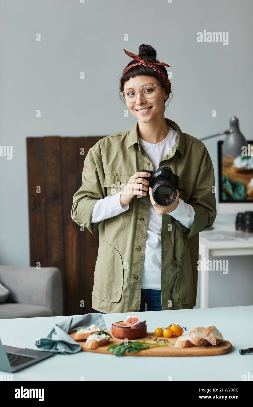 Vertical portrait of young female photographer smiling at camera while ...