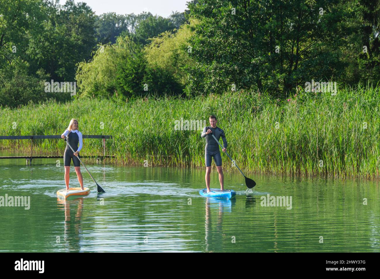 Two young people having fun while paddling with a SUP board on a lake ...