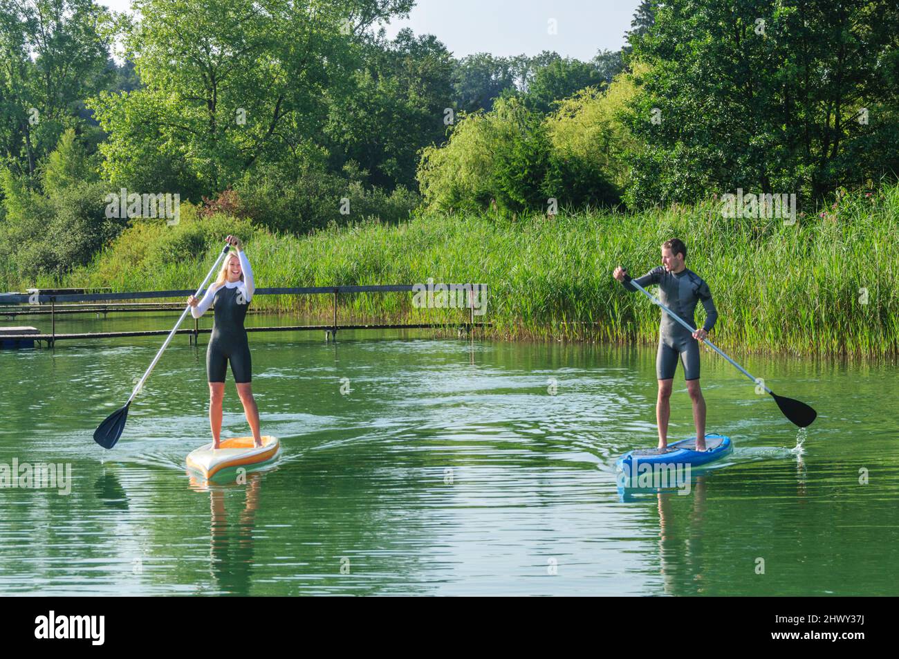 Two young people having fun while paddling with a SUP board on a lake ...