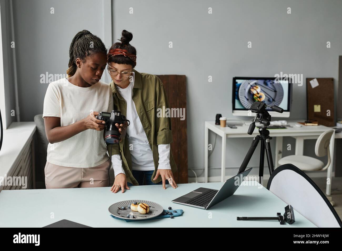 Portrait of two female photographers looking at photos in camera while ...