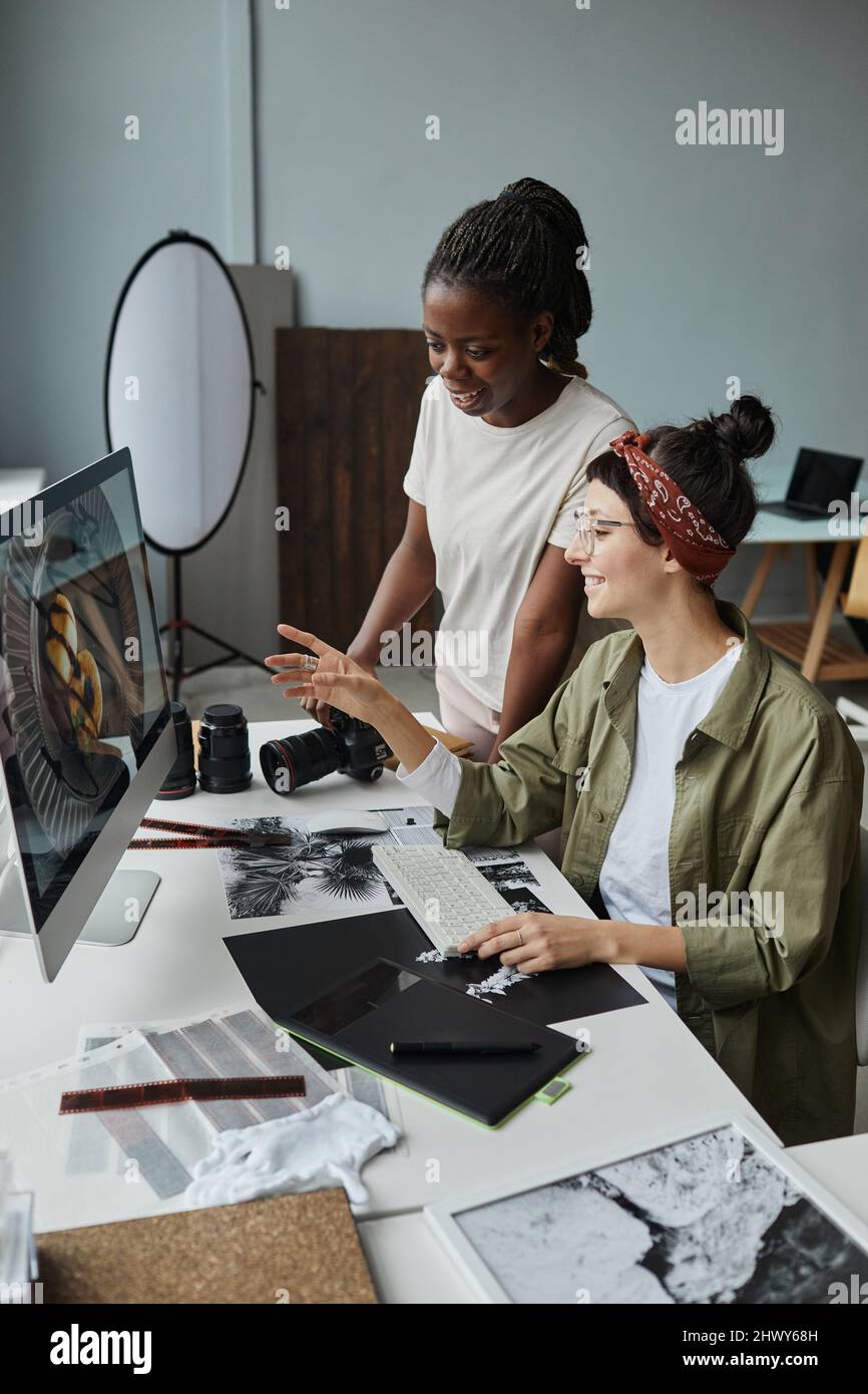 Vertical portrait of two smiling female photographers discussing images ...