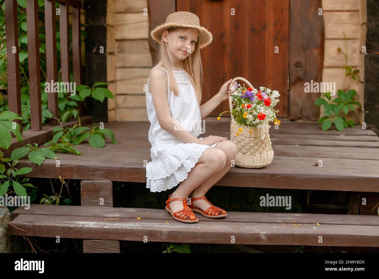 Playful tween girl sitting on doorstep of country house with basket of ...