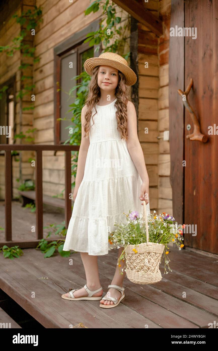 Smiling tween girl standing on doorstep of country cottage with basket ...
