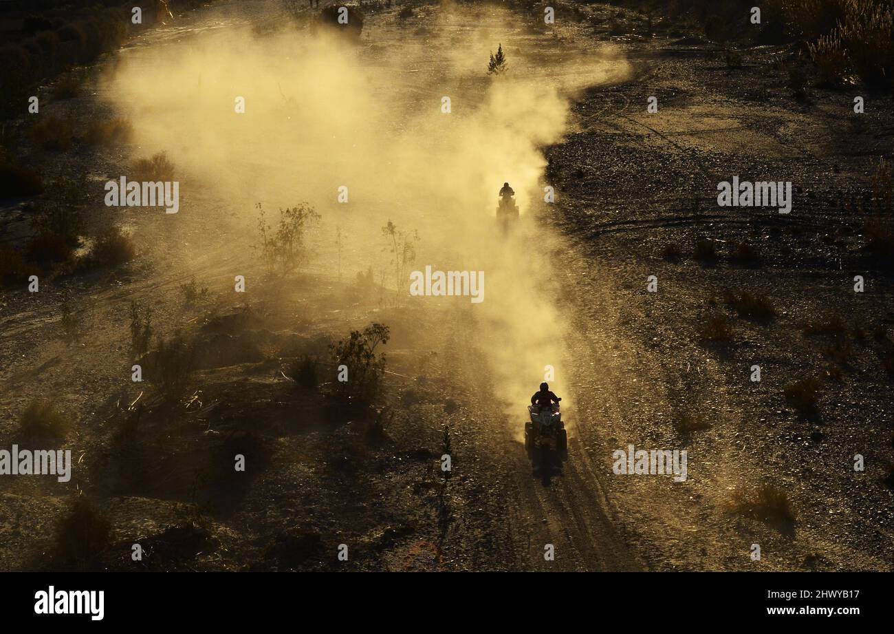Morning dust cloud, quad bike riders speeding through arid landscape of ...