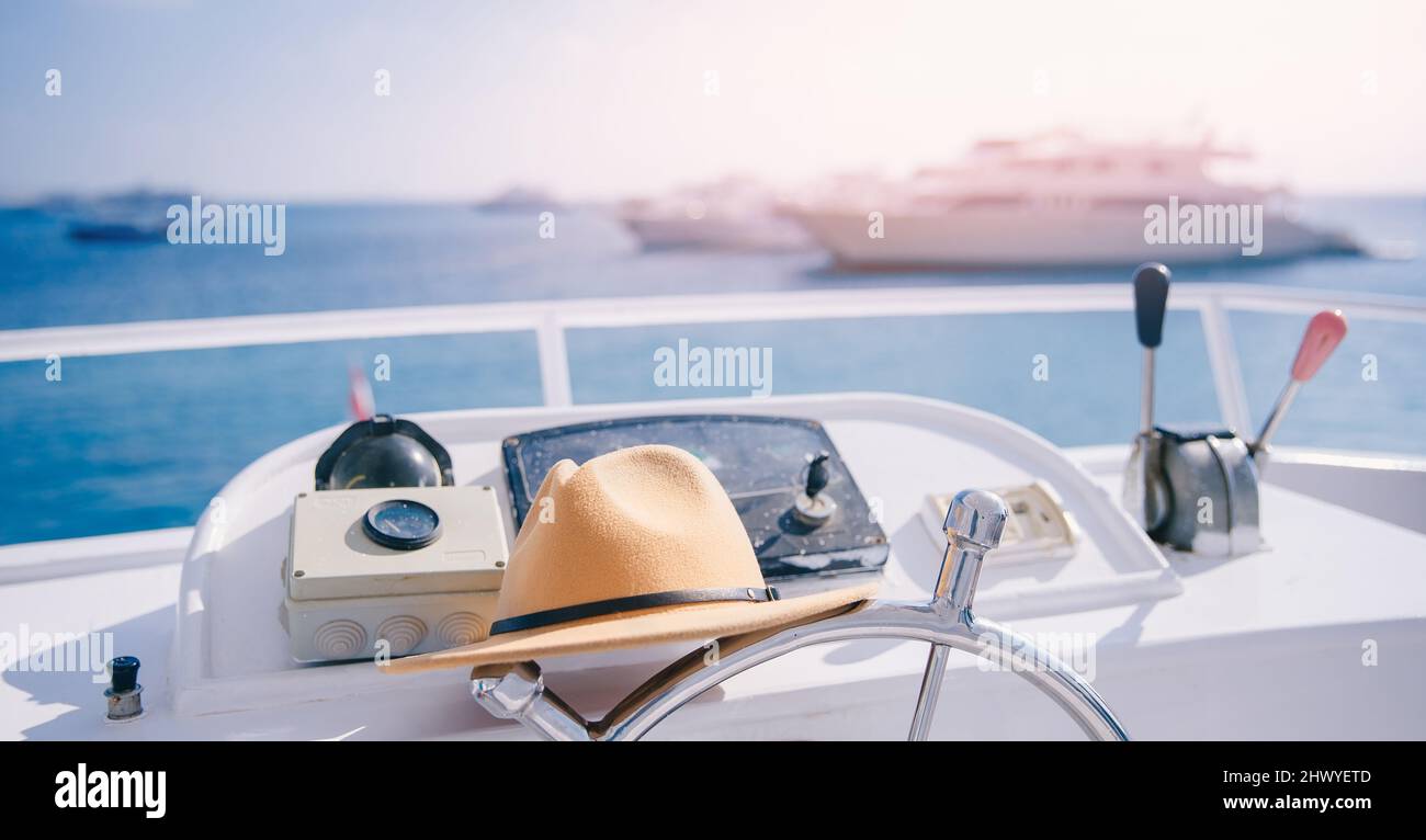 Travel hat lies on steering wheel of modern luxury yacht with sun light ...