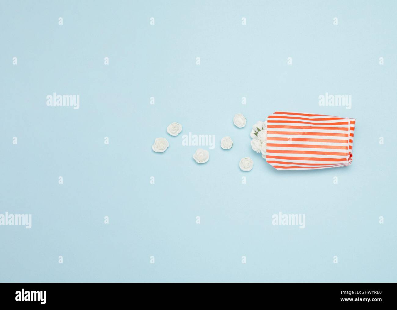 Flowers falling out of paper popcorn bag against pastel blue background ...