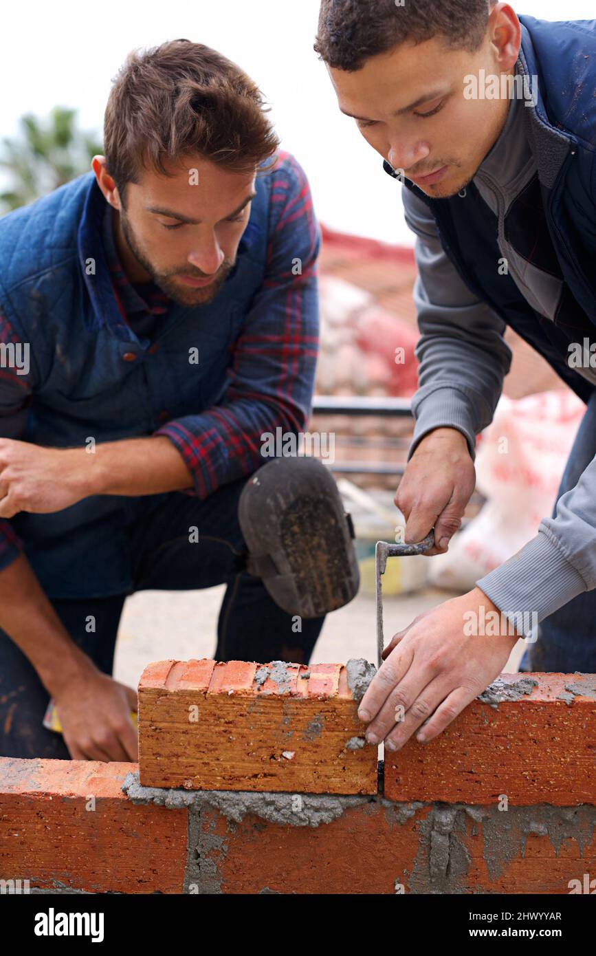 Showing the young one how its done. Shot of bricklayers at work Stock ...