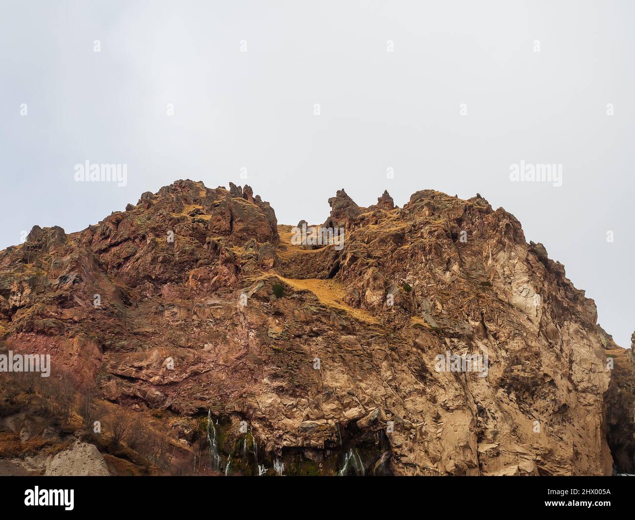 A massive steep rock with sharp rocky relief and streams of waterfalls ...