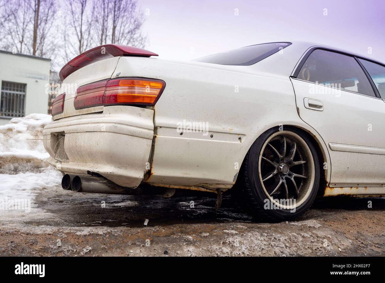 the back of a white smashed Japanese sedan with black rims with a ...