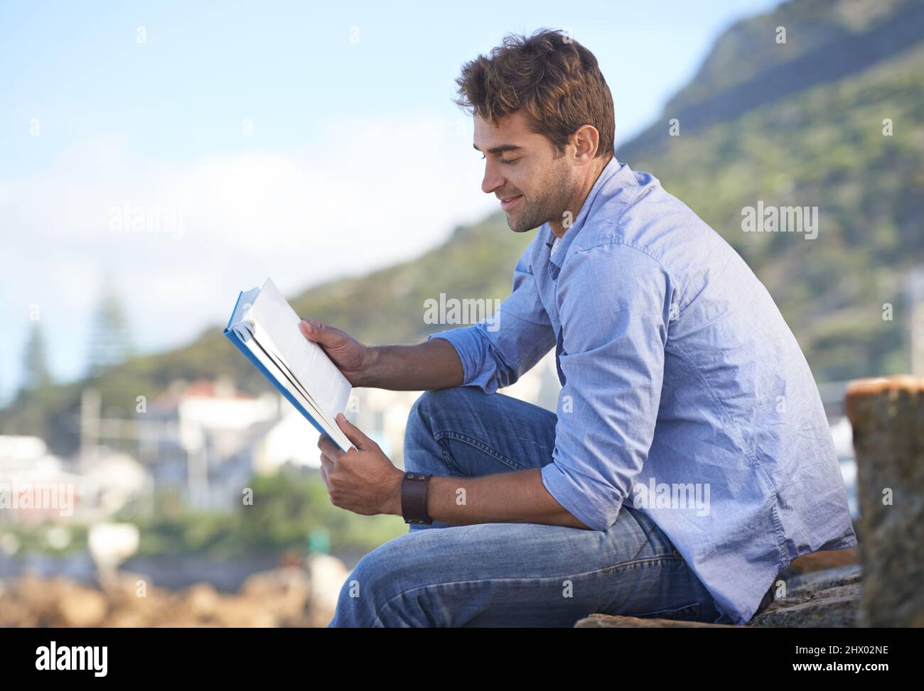 Novels are a great way to relax. A young man reading a book outdoors ...