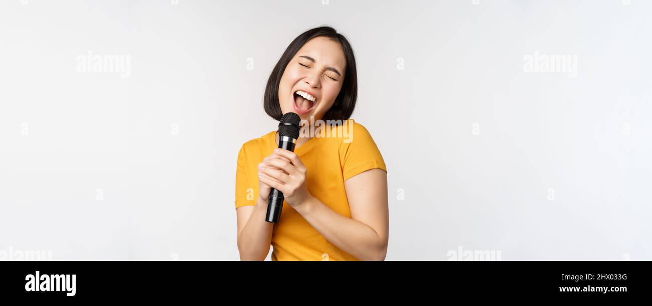 Happy asian girl dancing and singing karaoke, holding microphone in ...