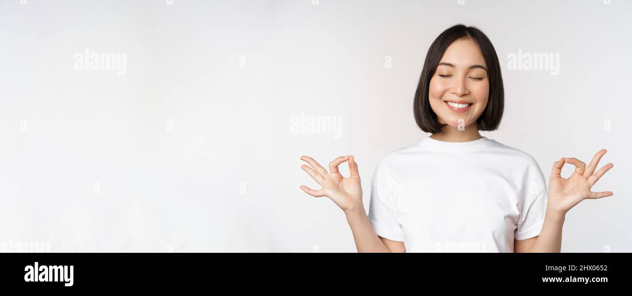 Portrait of young asian woman meditating, smiling pleased and practice ...
