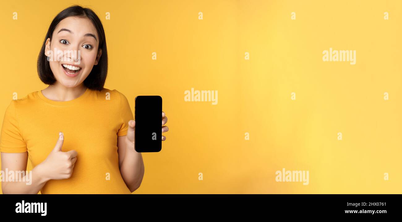 Excited asian woman showing mobile phone screen, thumbs up, like smth ...