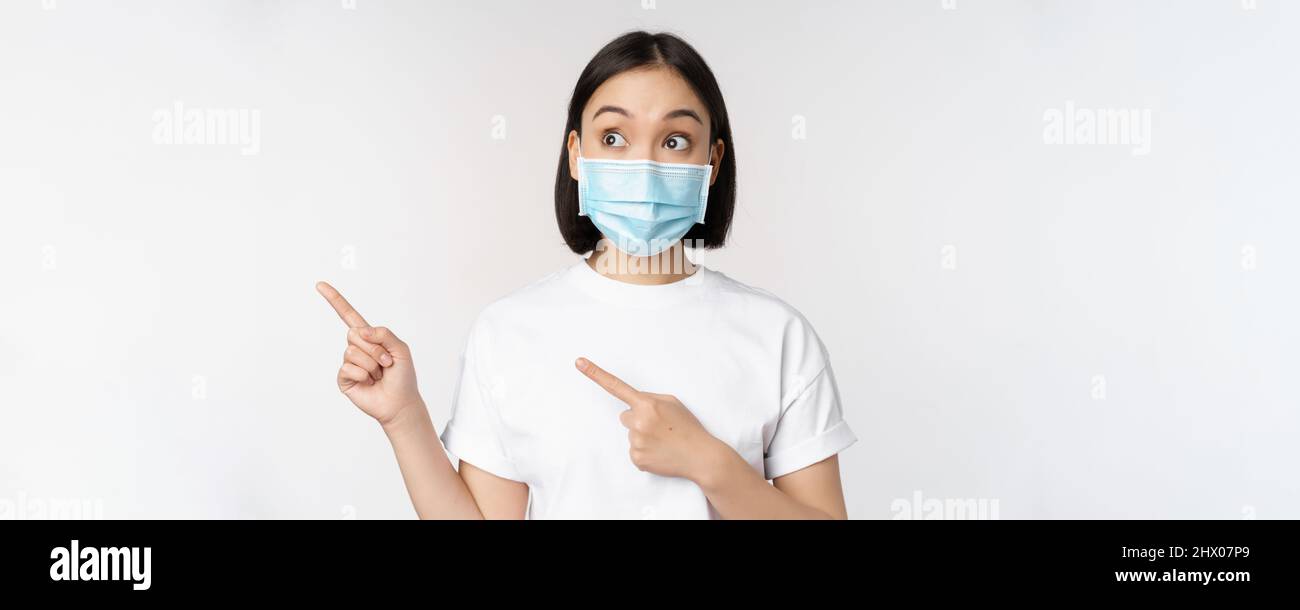 Young korean woman in medical face mask pointing fingers left and ...