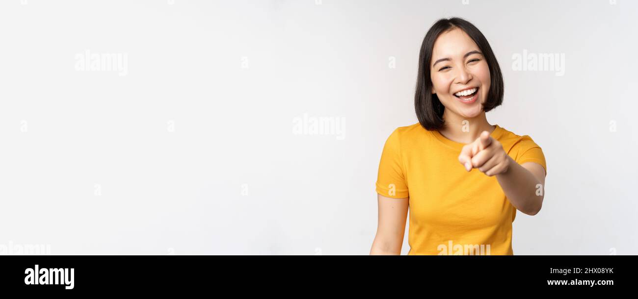 Happy beautiful asian woman laughing, pointing finger at camera and ...
