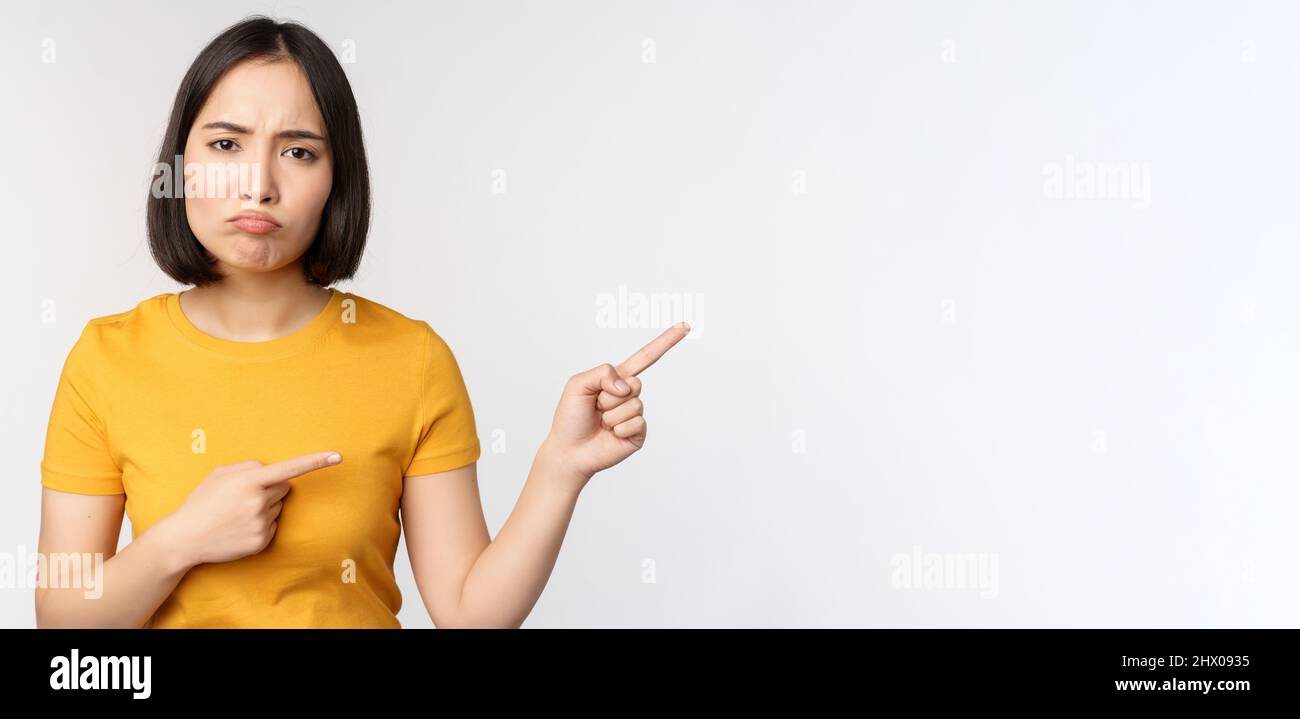 Portrait of disappointed, moody asian girl, pointing fingers right and ...
