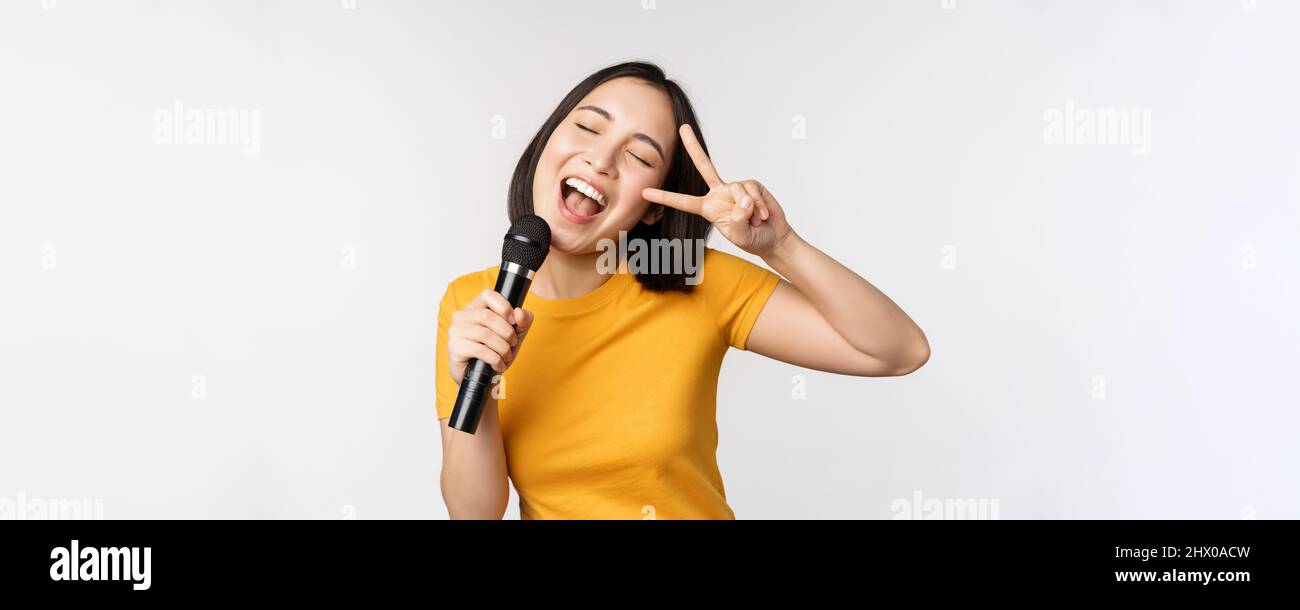 Happy asian girl dancing and singing karaoke, holding microphone in ...