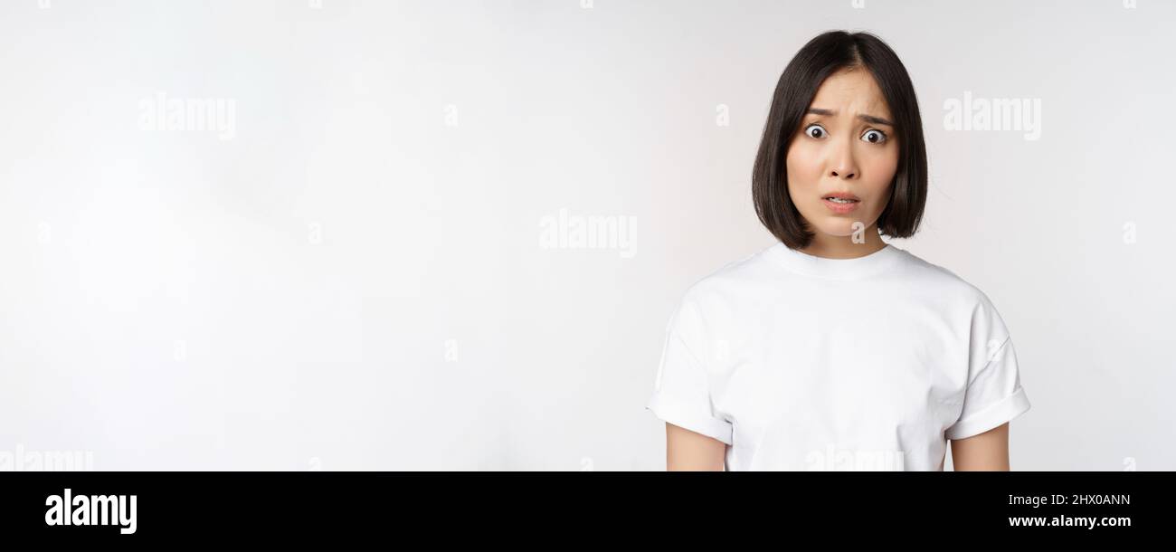 Image of shocked and frustrated asian woman, looking alarmed at camera ...