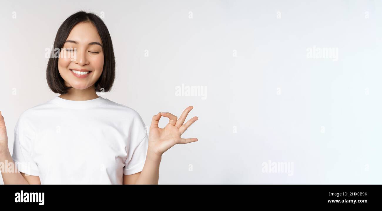 Portrait of young asian woman meditating, smiling pleased and practice ...