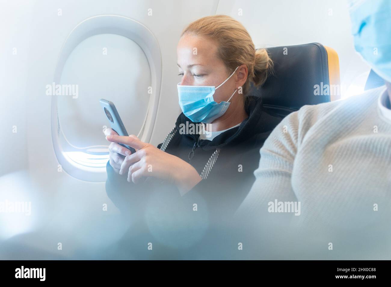 A young woman wearing face mask, using smart phone while traveling on ...