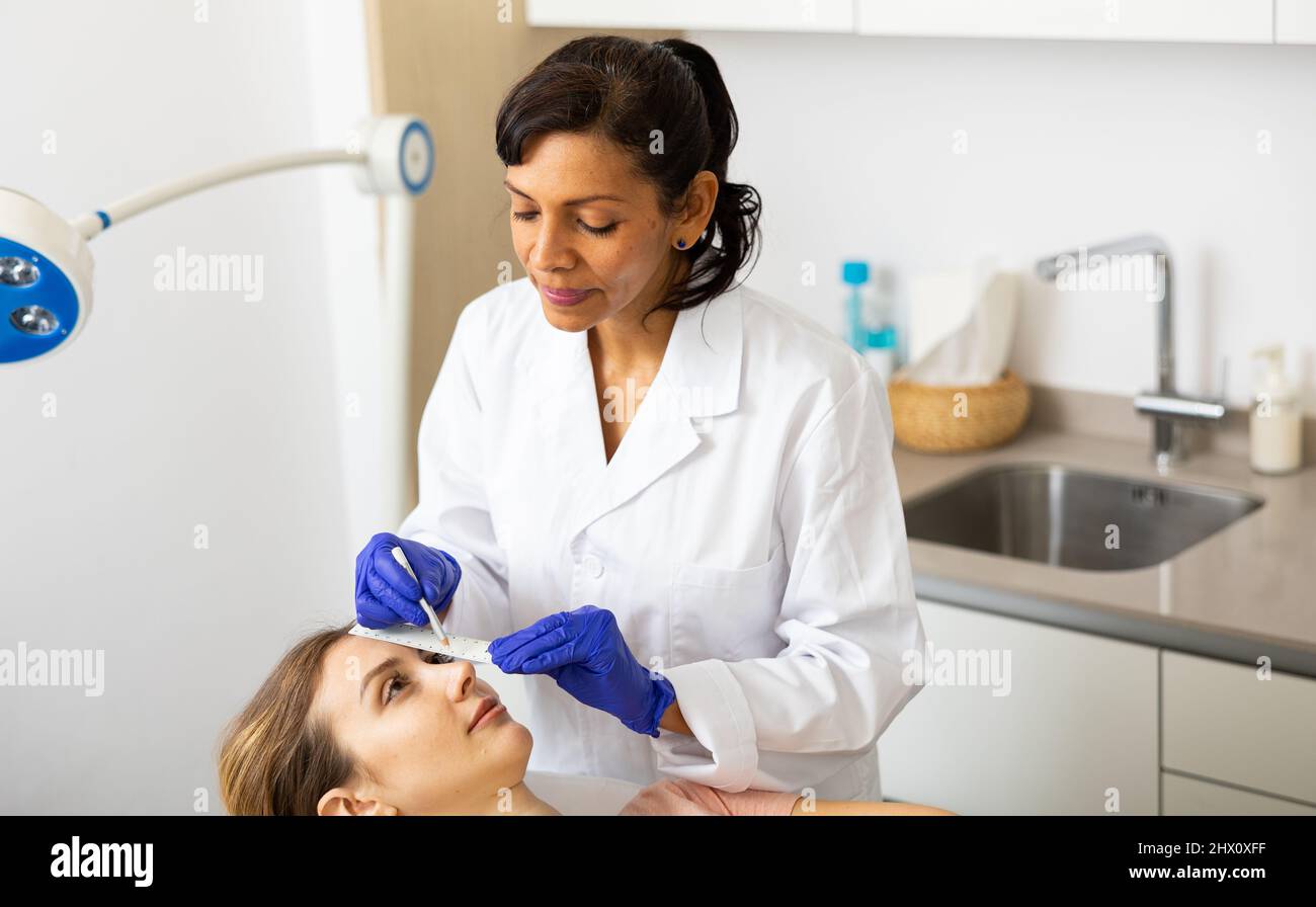 Beautician drawing correction lines on woman face Stock Photo - Alamy